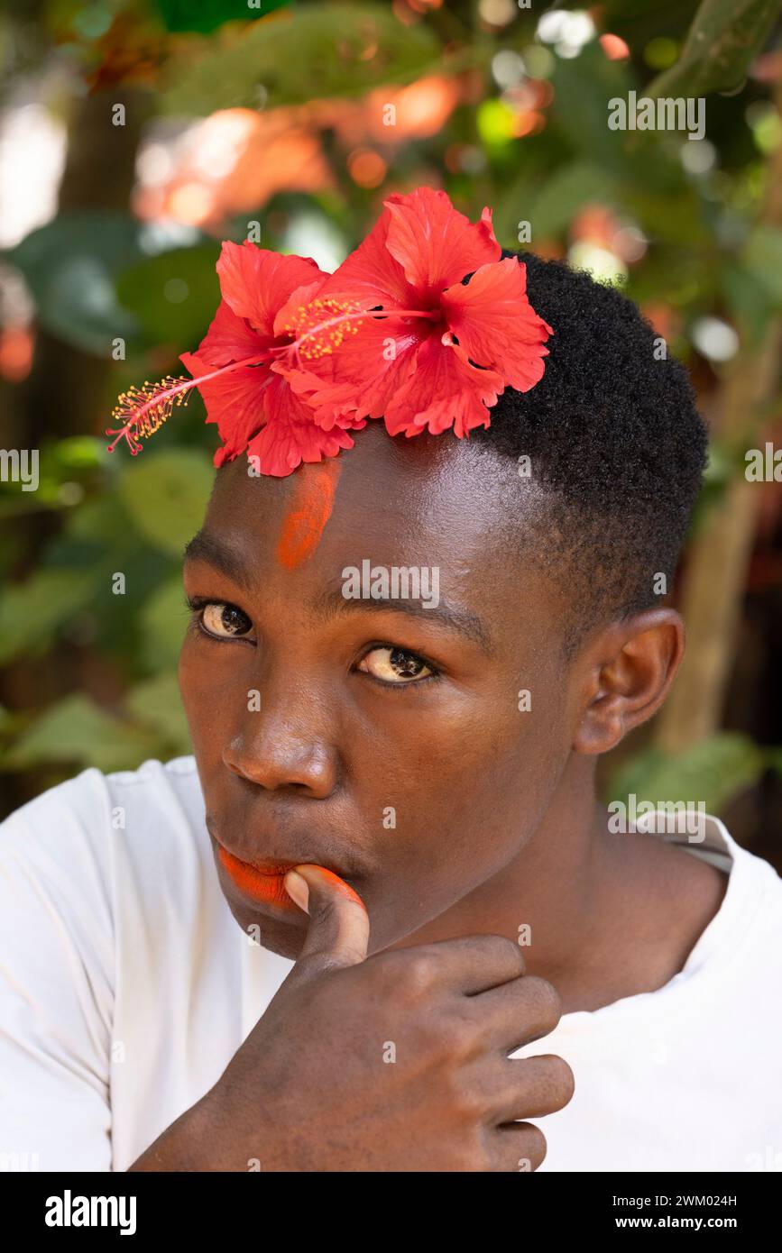 Young Swali painting her lips with Achiote, two red hibiscus flowers in ...