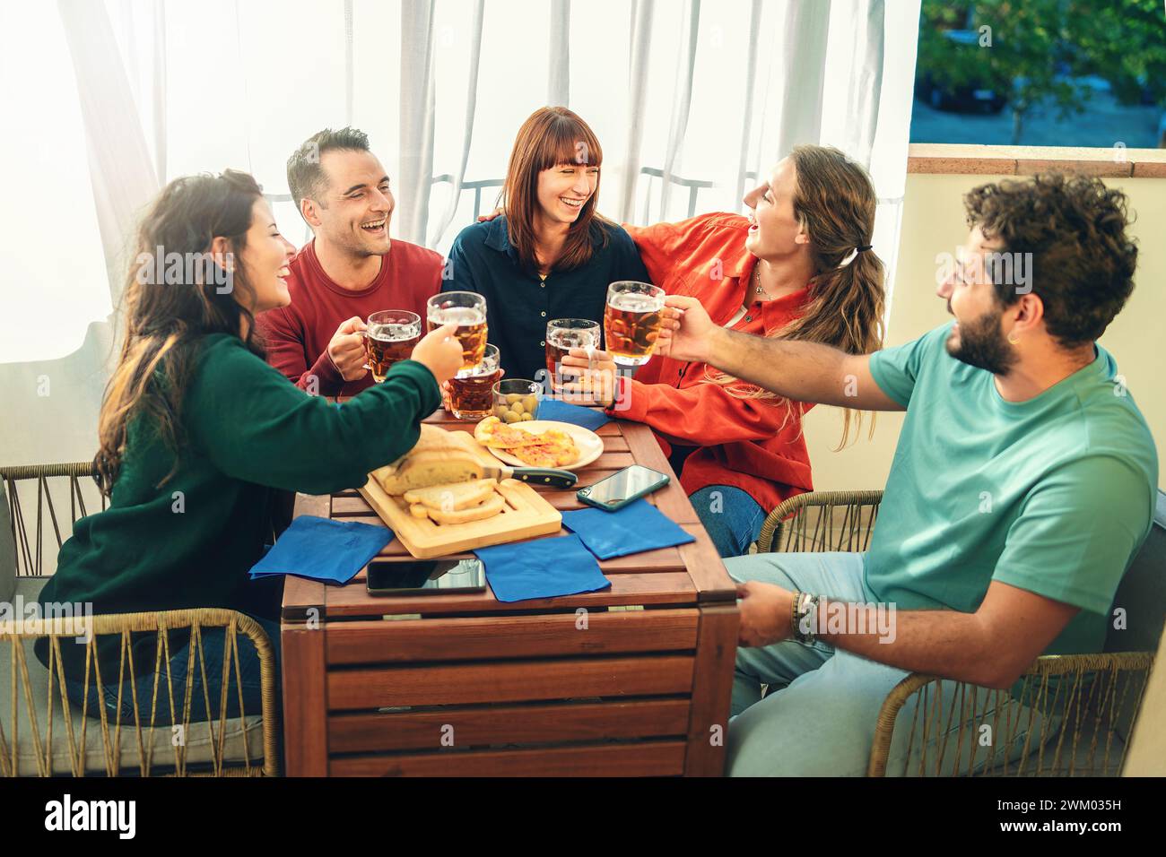 Group of cheerful friends toasting with beer glasses at a casual home ...