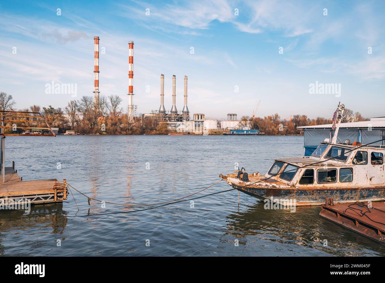 A factory by the river emits pollution into the water, with rusty ships ...