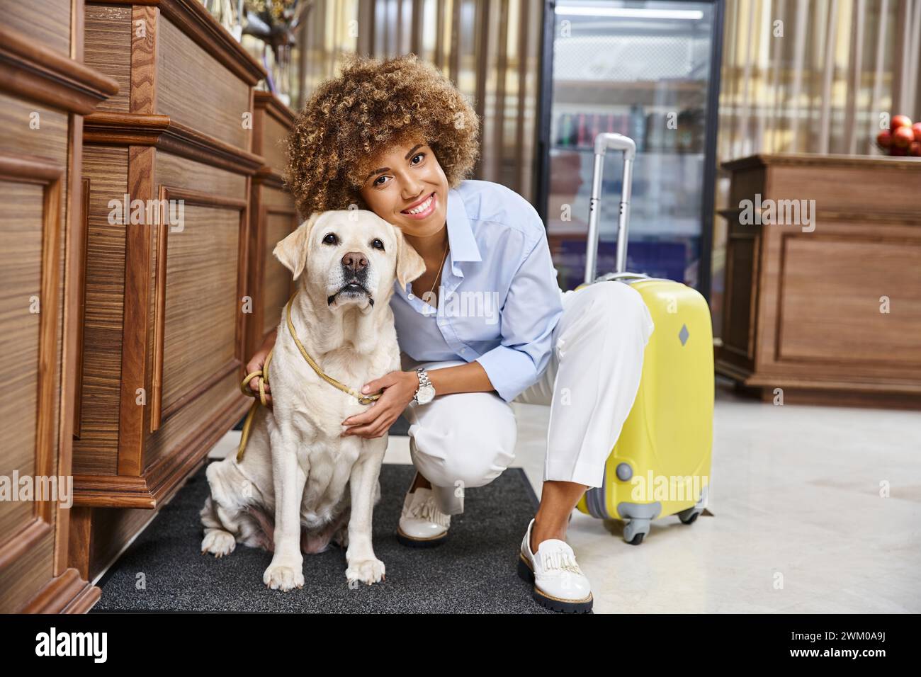cheerful african american woman cuddling labrador near suitcase in ...