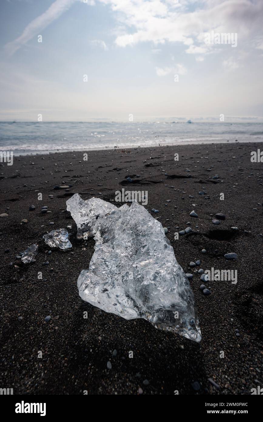 Ocean waves lapping up chunks of ice sparkling in the sun on a black ...