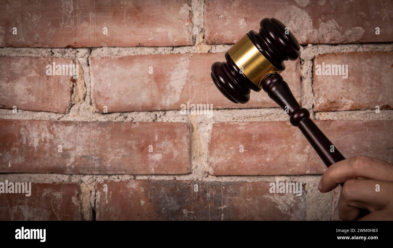 Judge hand holding gavel. Red brick background Stock Photo - Alamy