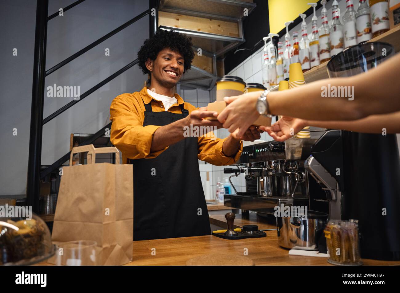 Happy barista handing over takeaway tray to customer at counter in cafe ...