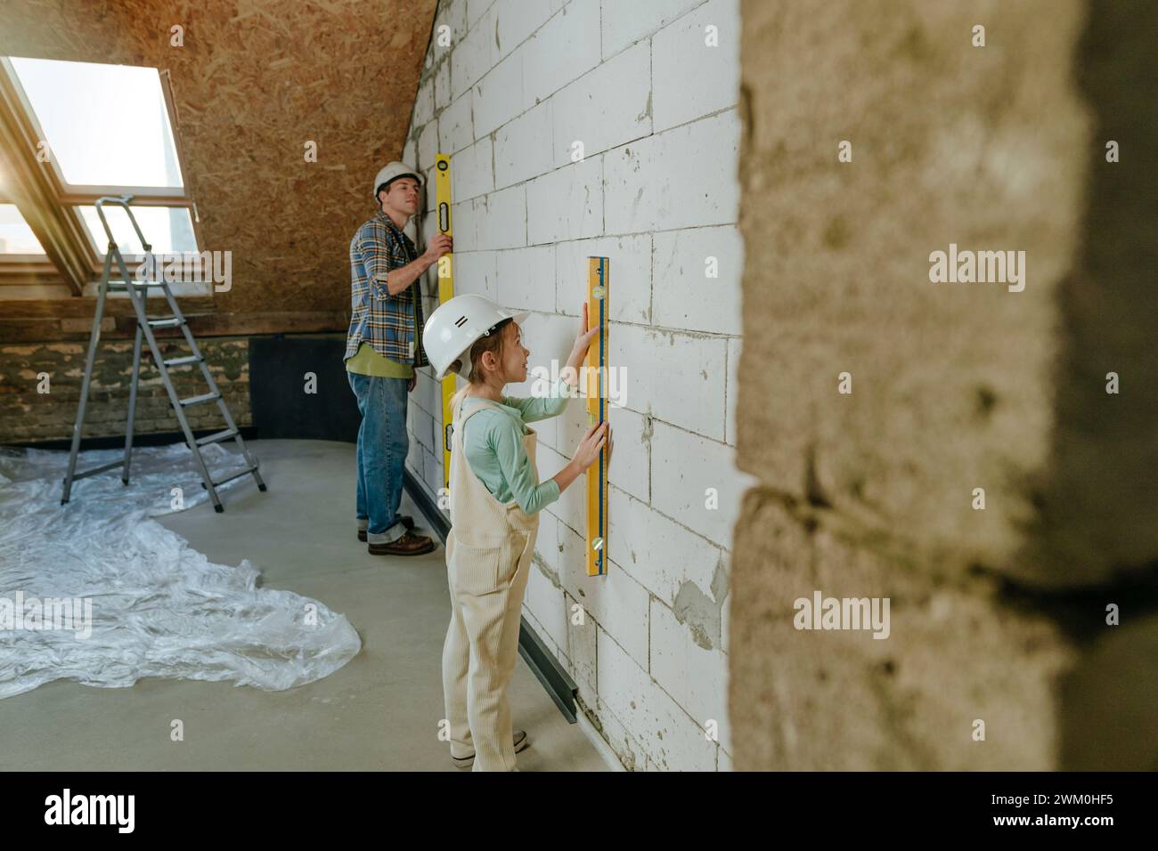 Girl wearing hardhat and measuring wall through leveling tool with ...