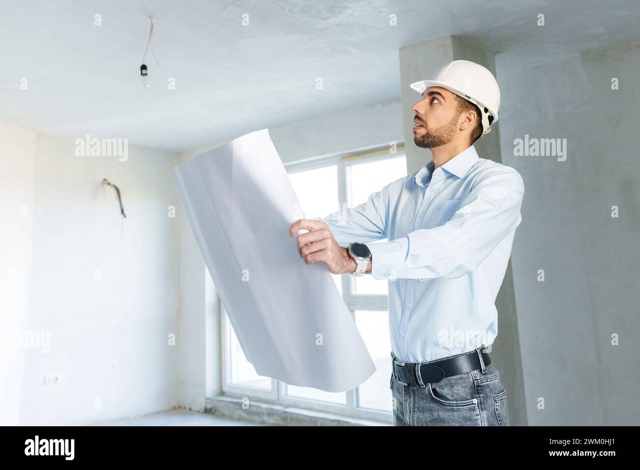 Architect with blueprint examining construction site Stock Photo - Alamy