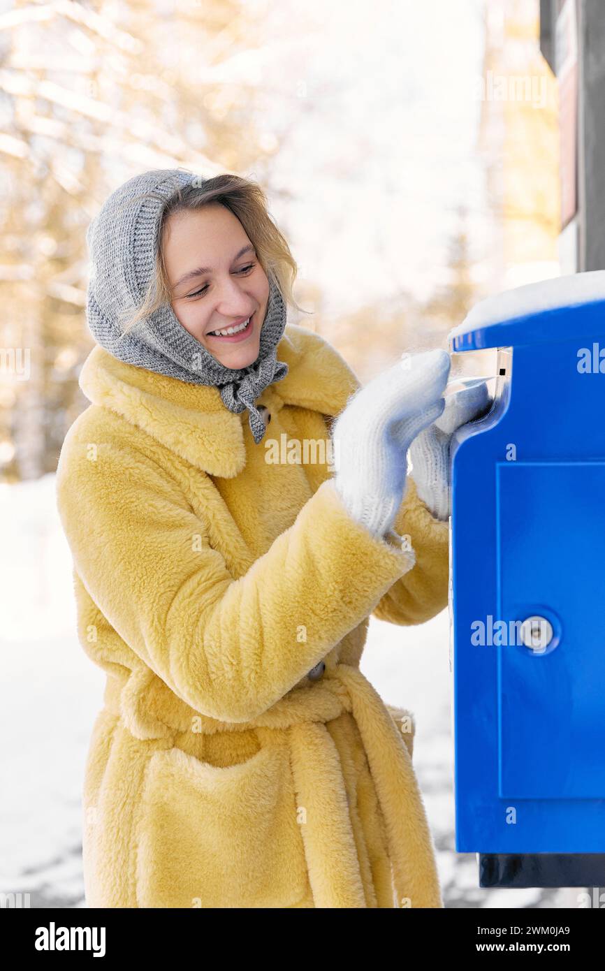 Happy young woman putting postcard in mailbox Stock Photo - Alamy