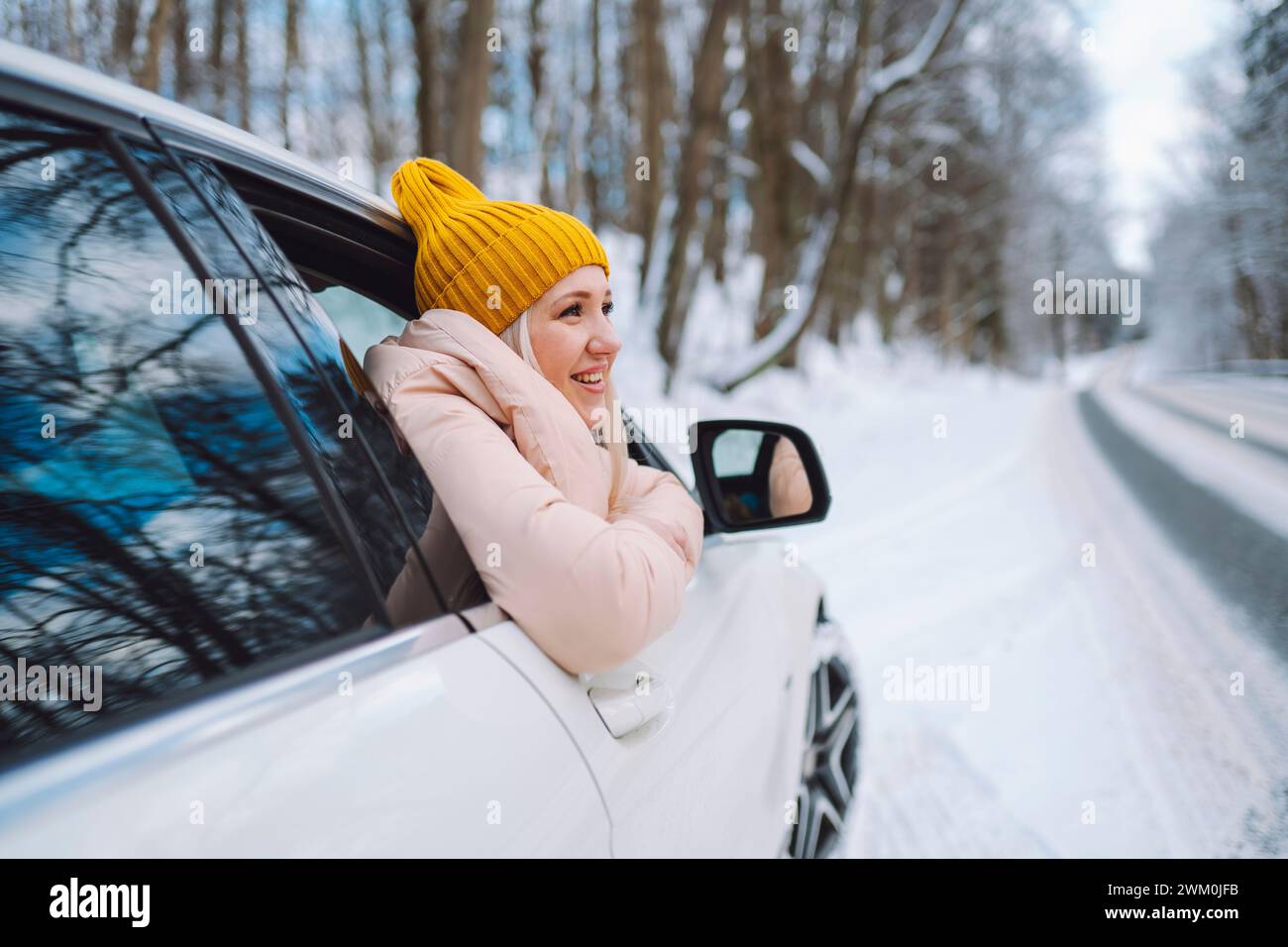 Woman wearing knit hat and leaning out of car window in winter forest ...