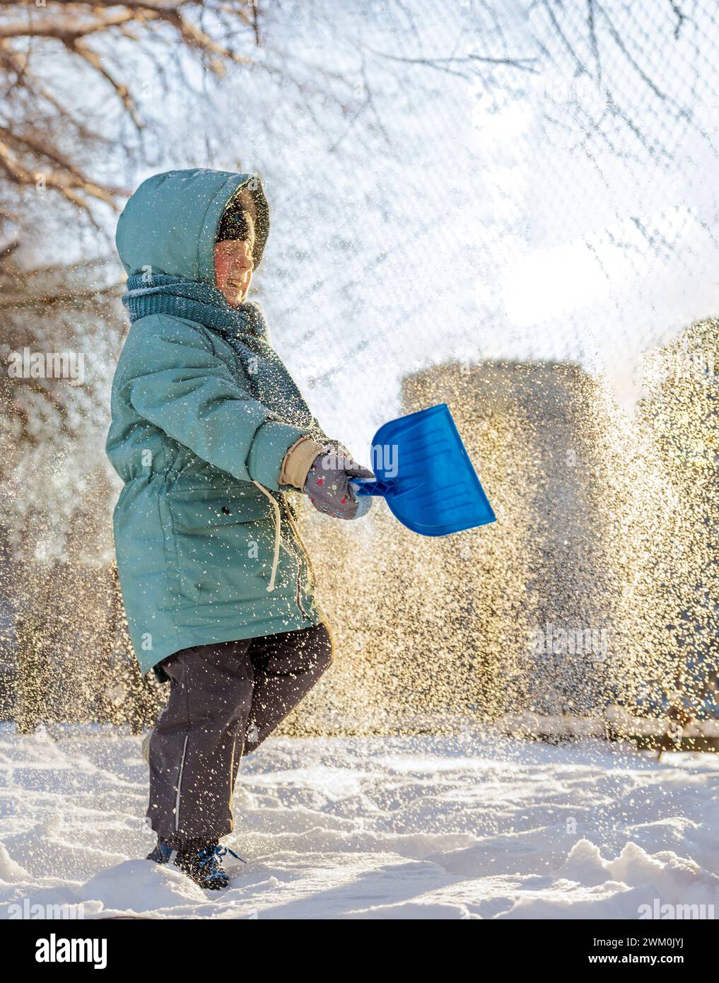 Boy wearing winter jacket and throwing snow with toy shovel Stock Photo ...