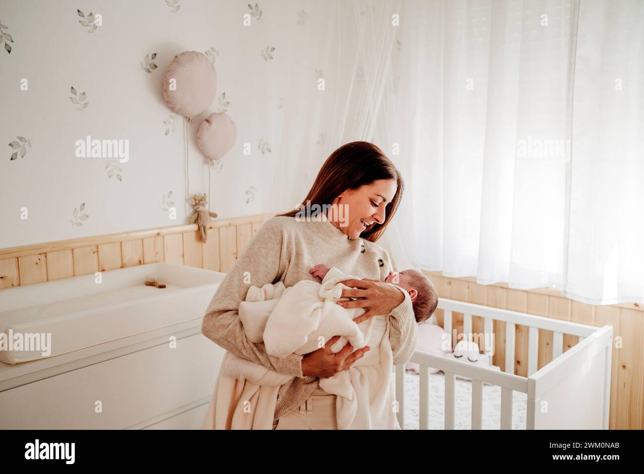 Happy mother holding baby girl in arms near crib at home Stock Photo - Alamy