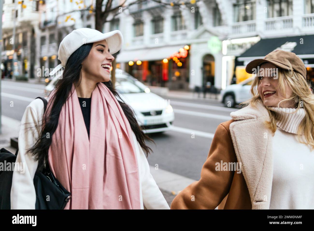 Cheerful friends wearing caps and walking at street in city Stock Photo ...