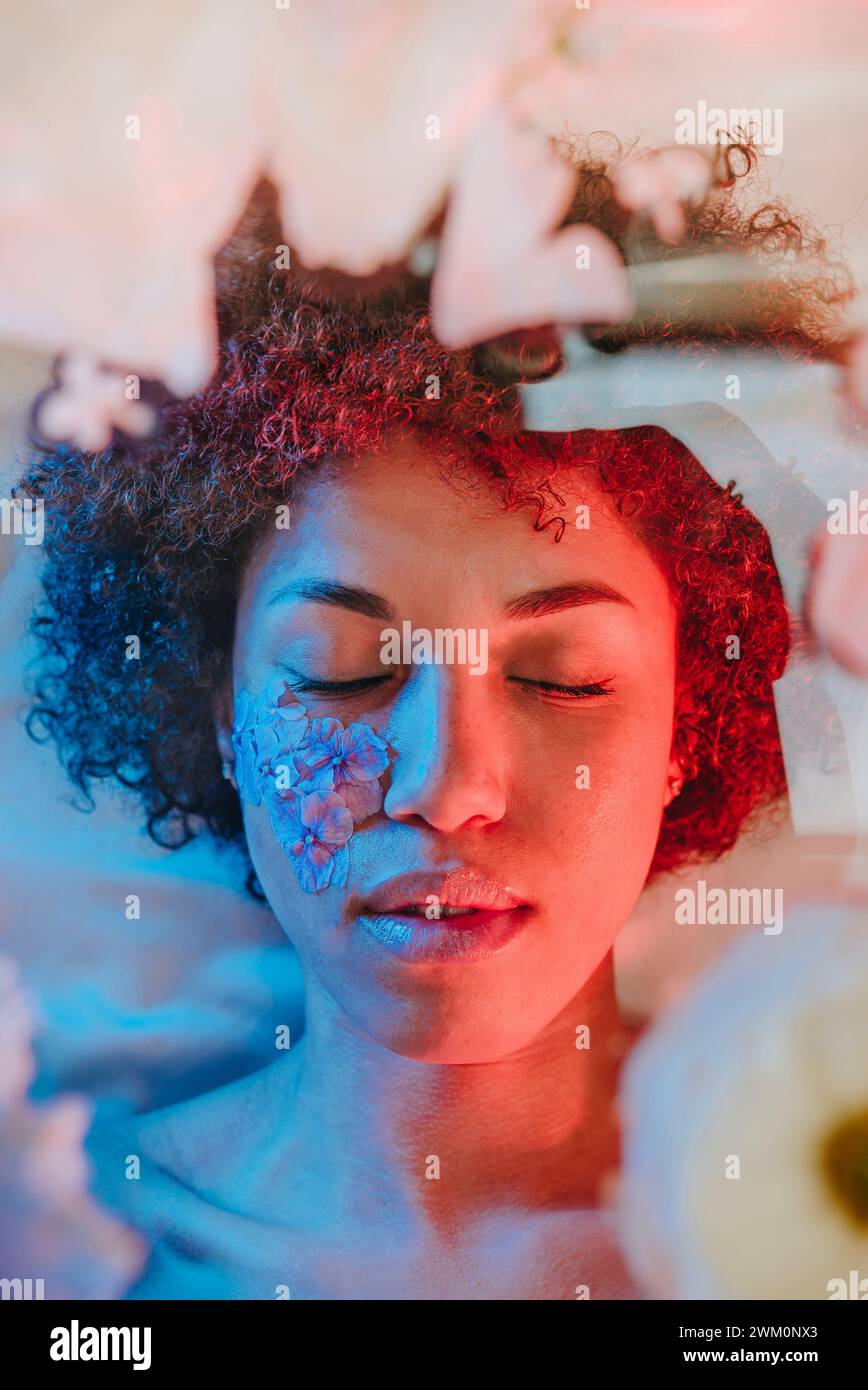 Beautiful woman with eyes closed lying below glass surface under neon ...