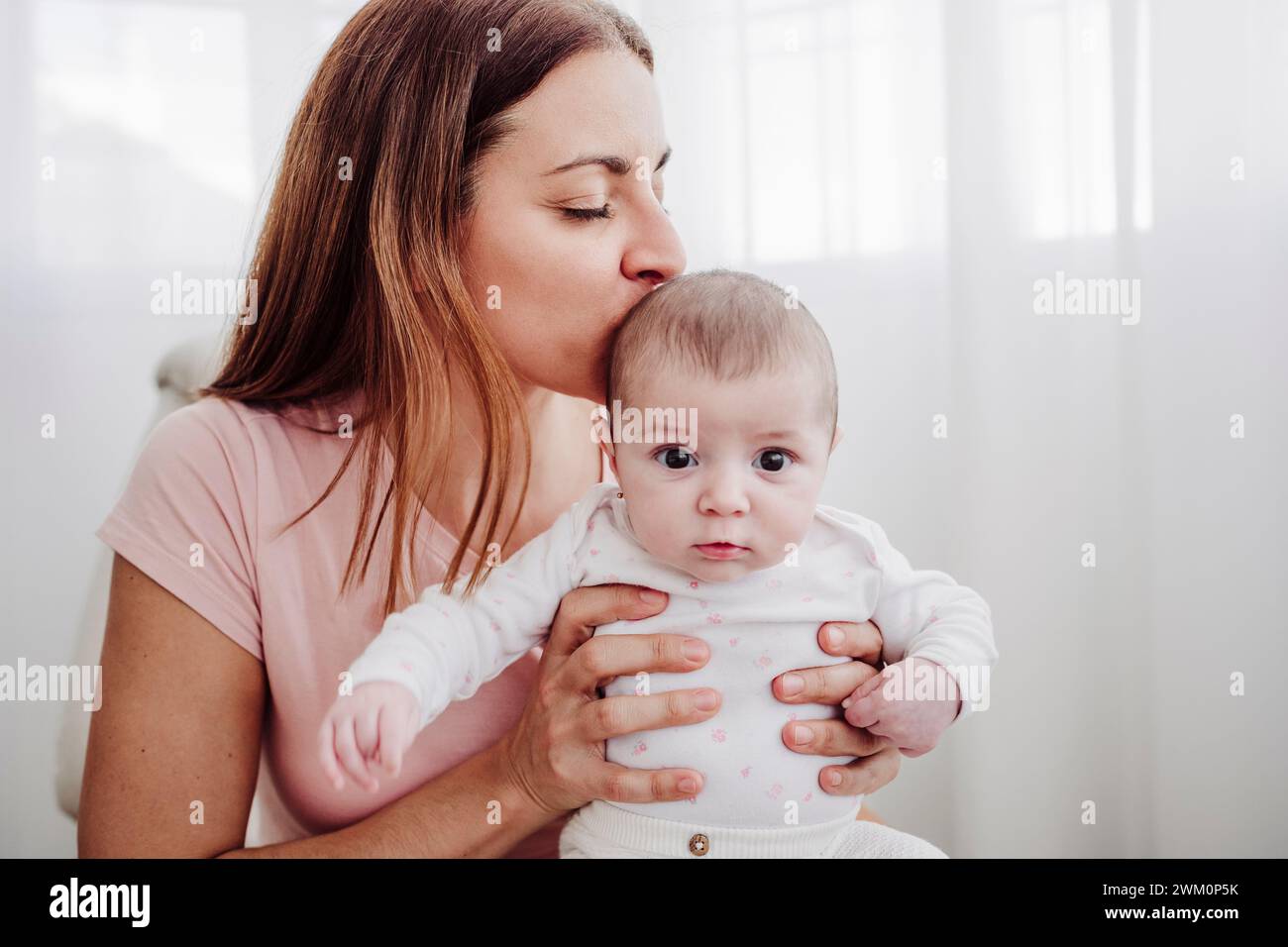 Mother kissing baby girl on head at home Stock Photo - Alamy