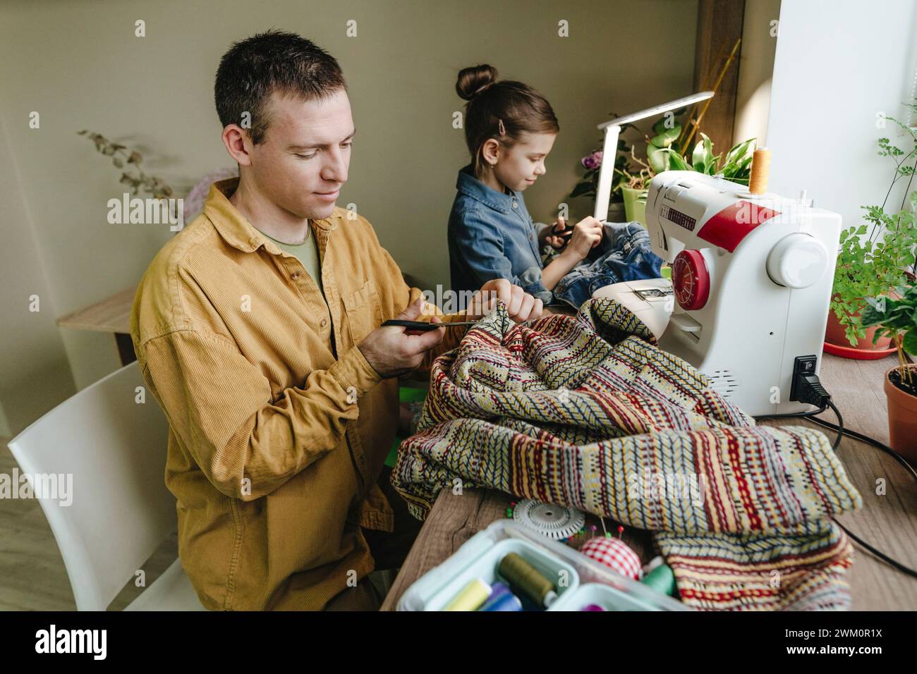 Father and daughter cutting fabrics with sewing machine on table at ...