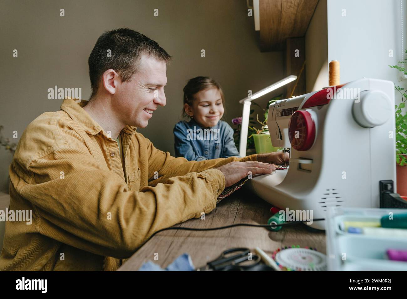 Happy daughter with father sewing recycled clothes through machine at ...