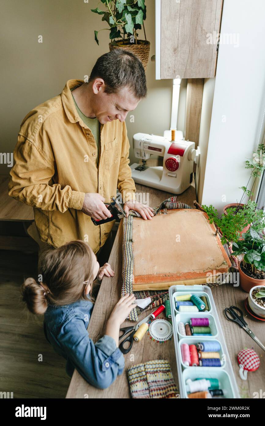Daughter and father securing fabric from old clothes on chair with ...