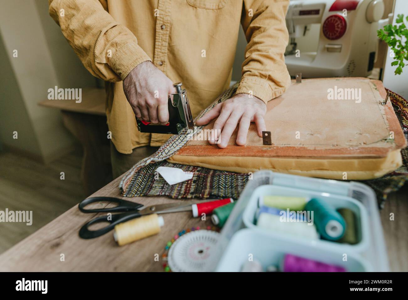 Man securing fabric from old clothes on chair with stapler at home ...