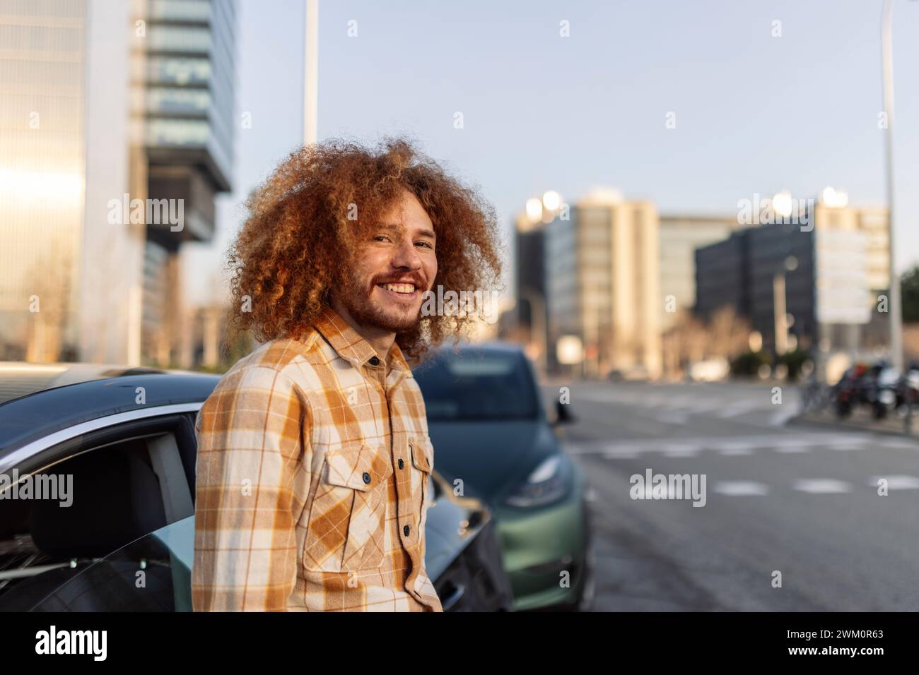 Happy curly man standing near cars on road Stock Photo - Alamy