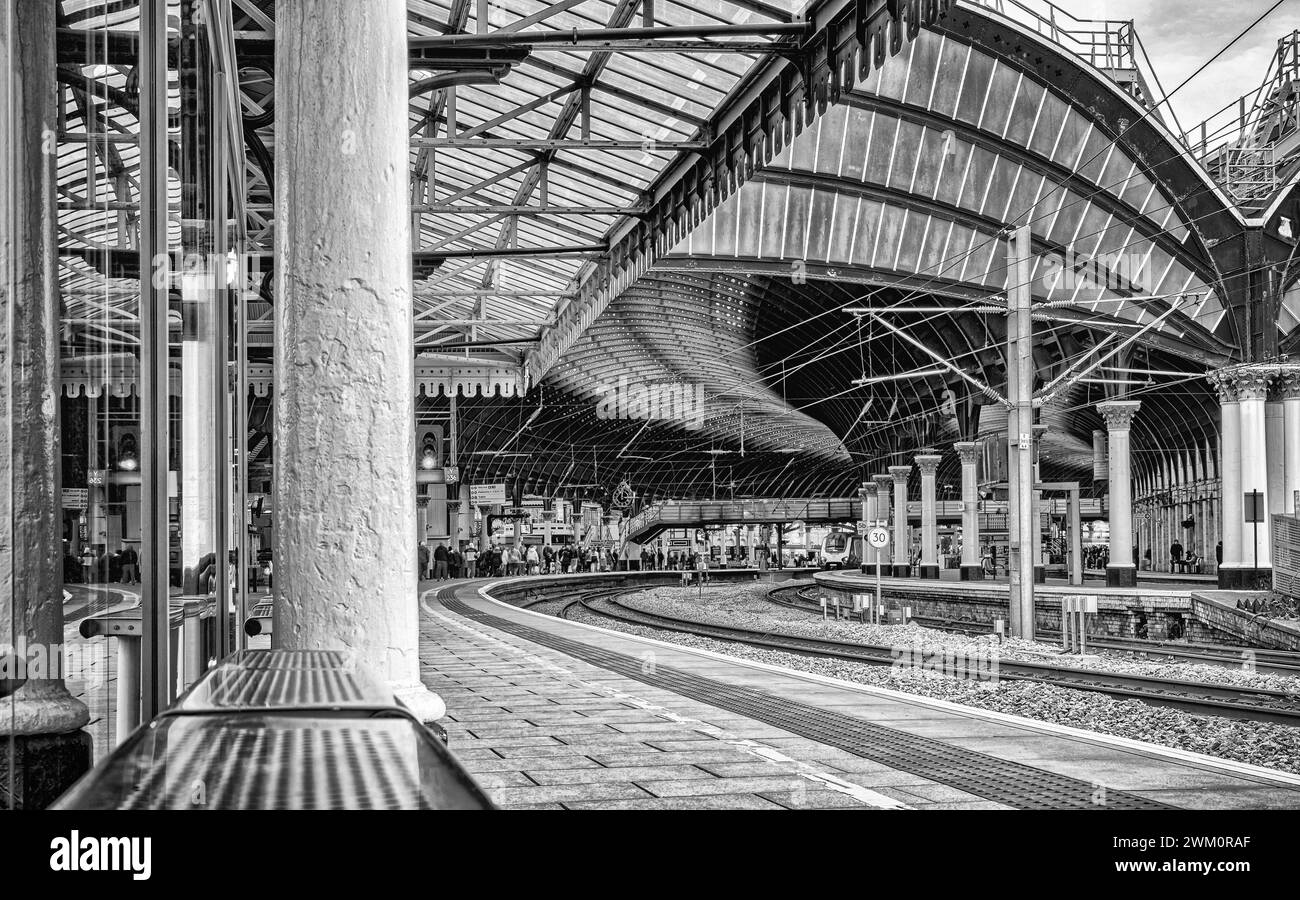 A historic metal arch covers the entrance to a railway station. A train ...