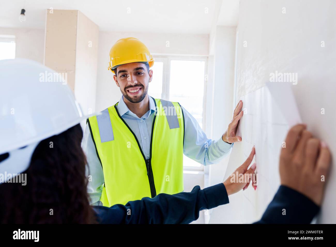 Smiling architect listening to colleague explaining blueprint at site ...