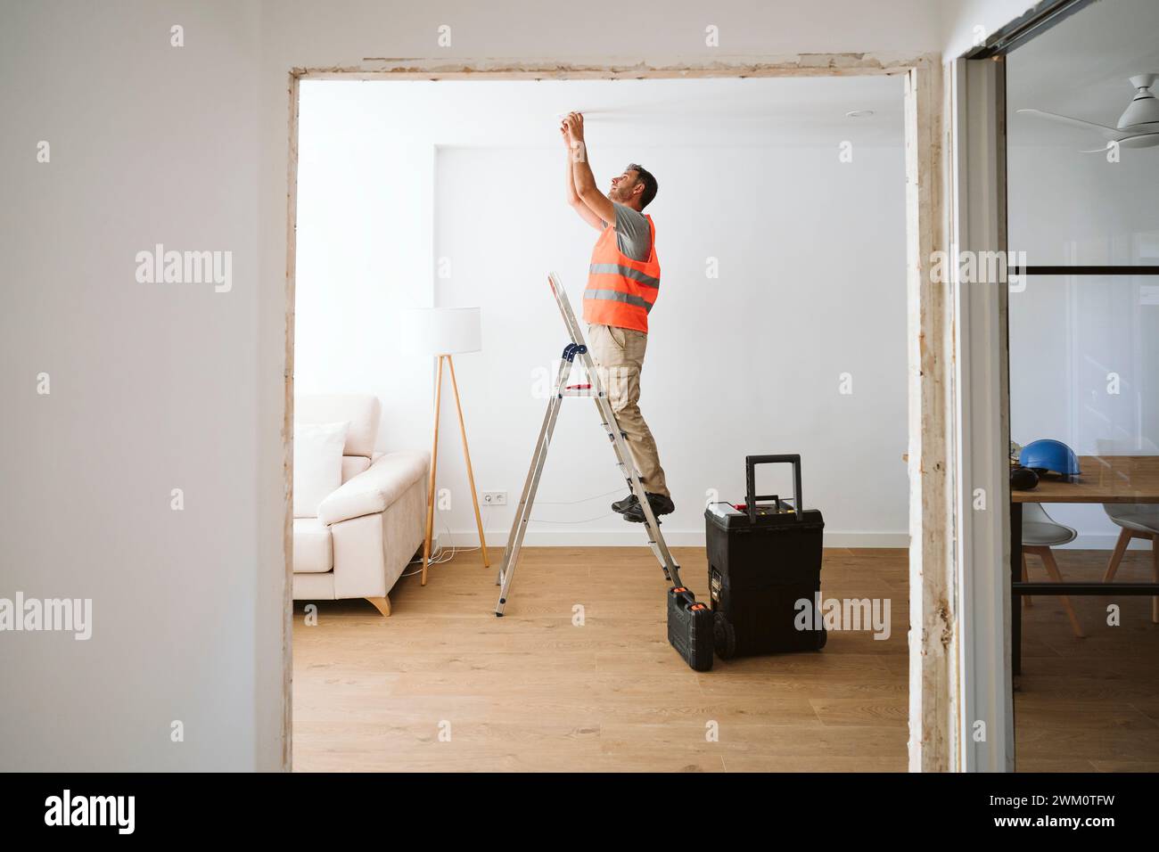 Repairman standing on ladder and working in house under renovation ...