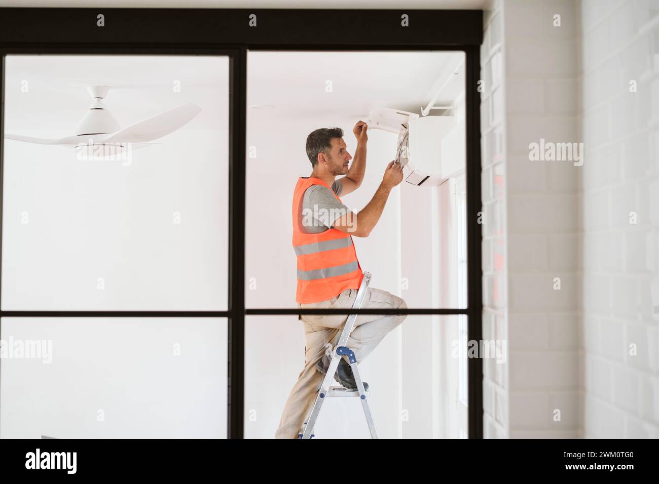 Technician standing on ladder and repairing air conditioner at home ...