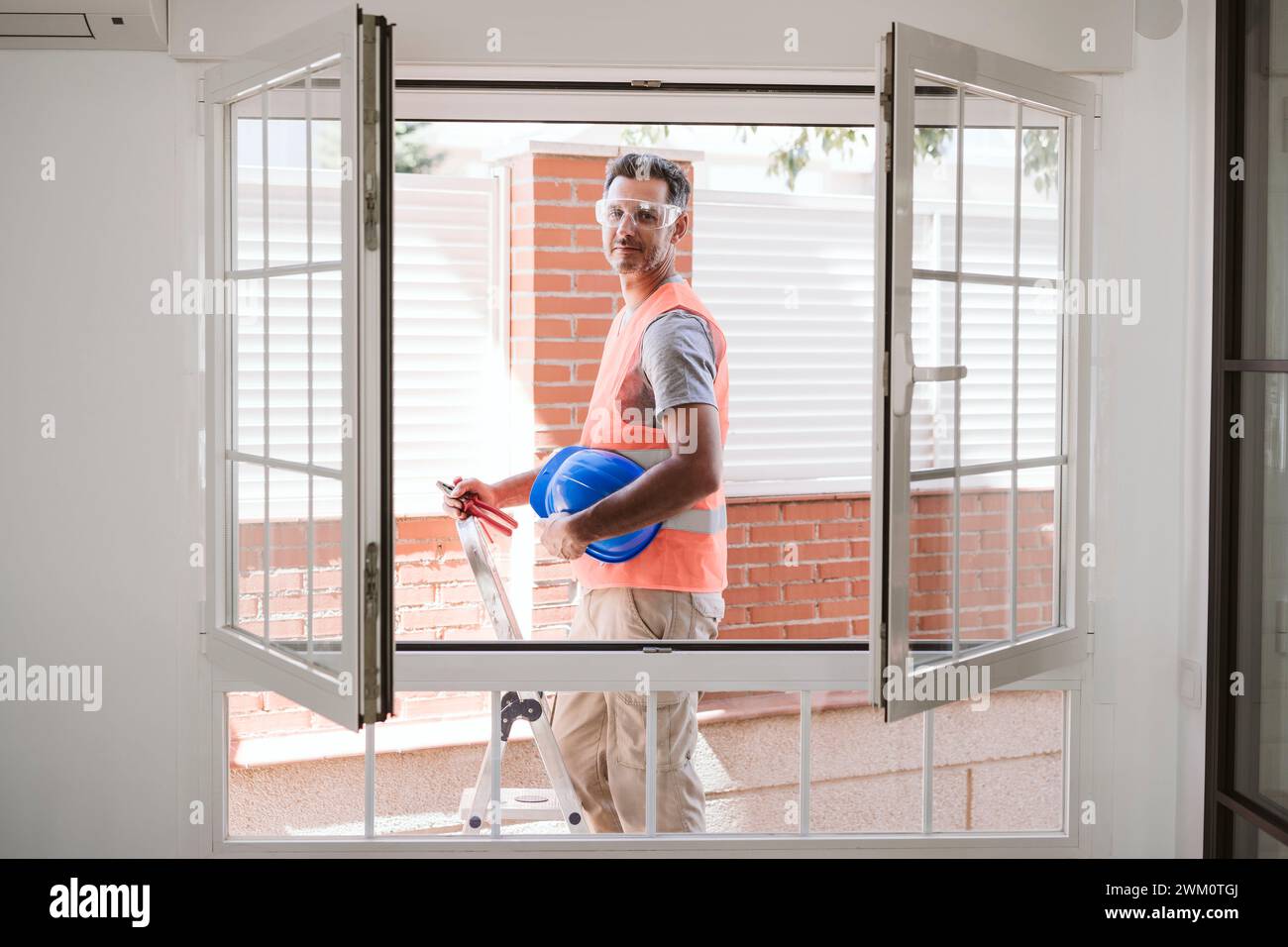 Mature repairman standing on ladder near window Stock Photo - Alamy