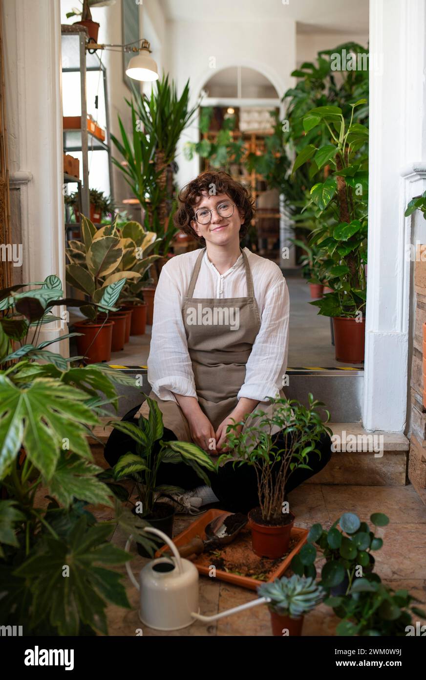 Smiling plant shop owner sitting with plants at nursery Stock Photo - Alamy