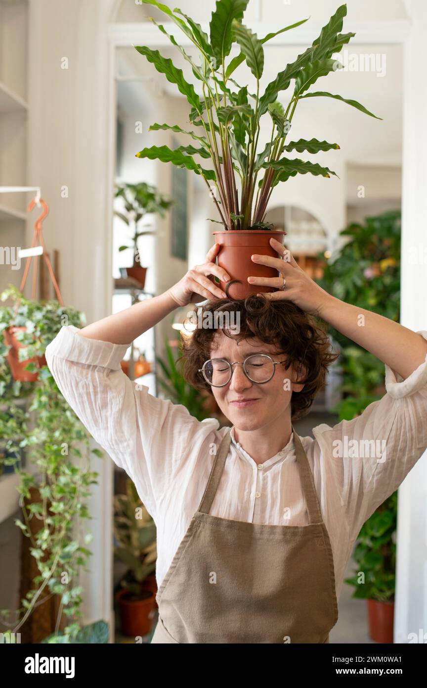 Smiling botanist with eyes closed holding plant over head in nursery ...