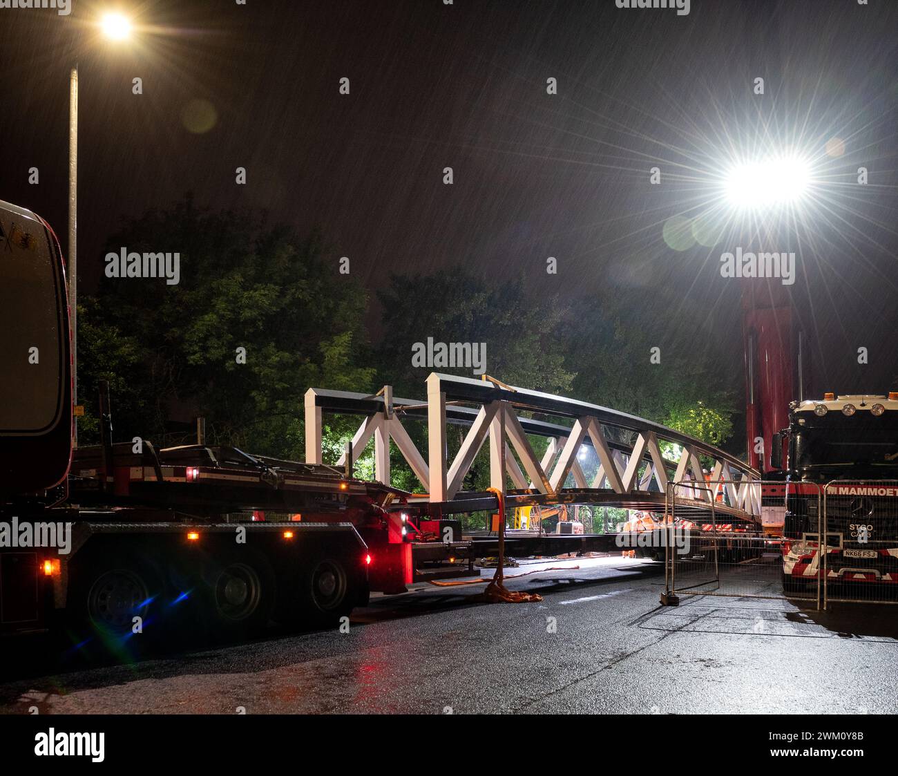 A completed pedestrian bridge is craned from height into place at night ...