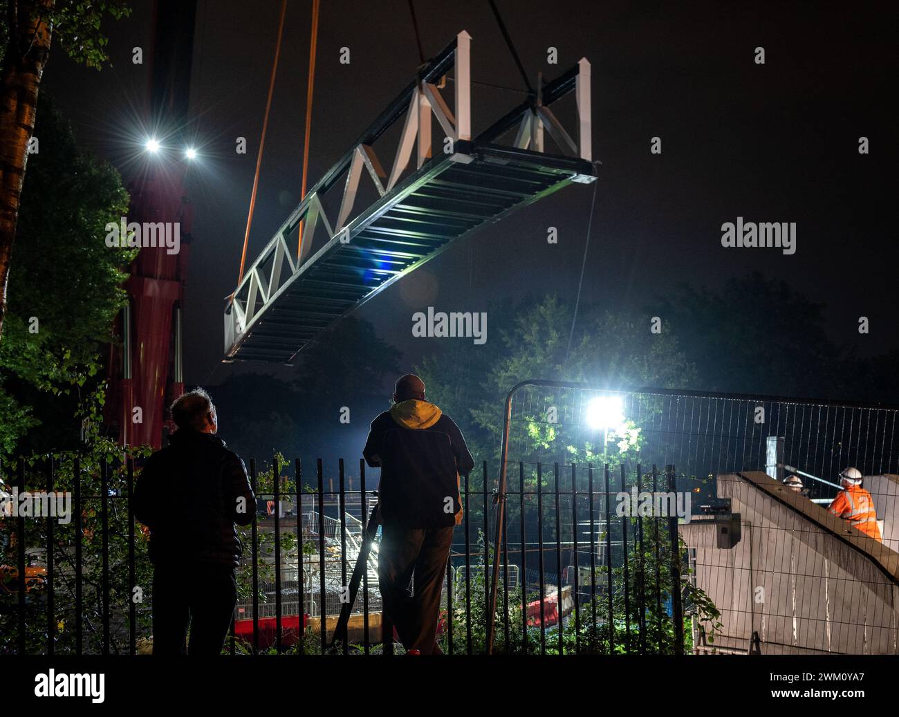 A completed pedestrian bridge is craned from height into place at night in Strathbungo, Glasgow ...