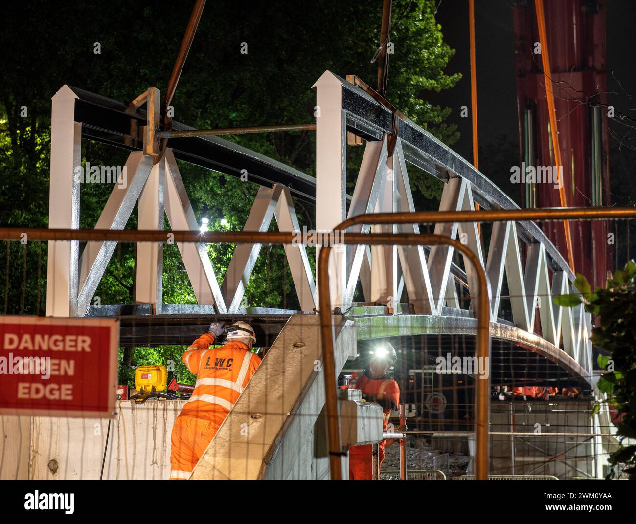 A completed pedestrian bridge is craned from height into place at night ...