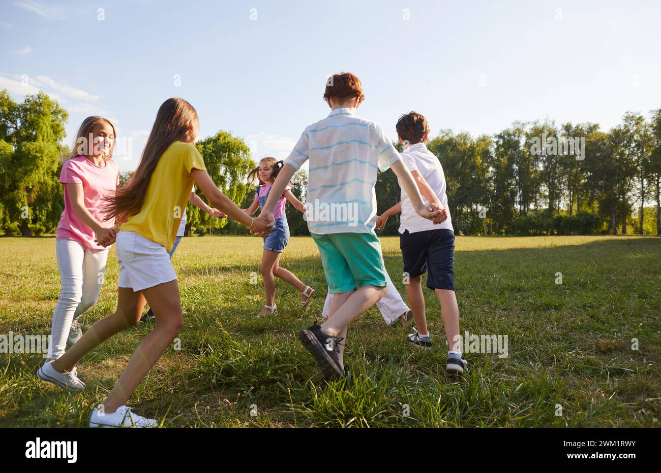 Group of happy, carefree children dancing a round dance in a green park ...