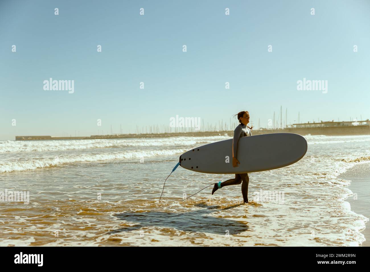 Happy female surfer in wetsuit with his surfboard entering out of sea ...