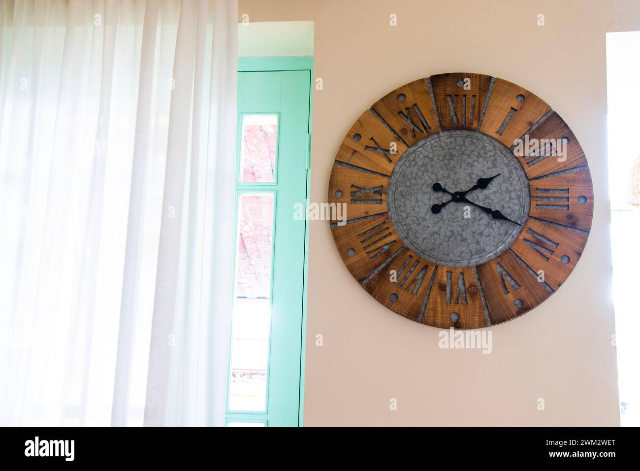Large clock hanging on wall next to window Stock Photo - Alamy