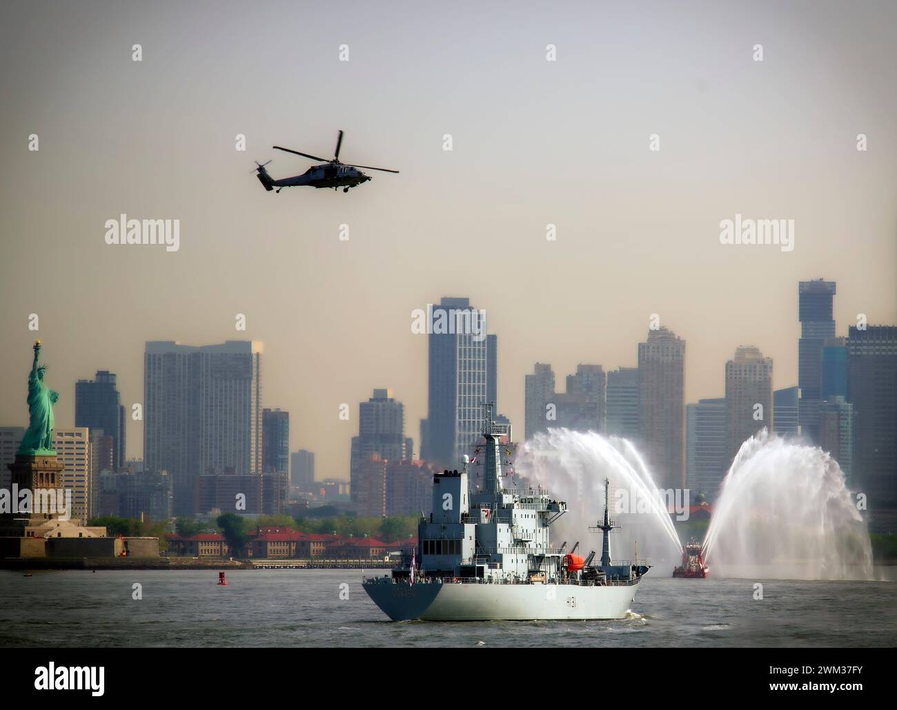 HMS Scott, hovering helicopter and tugboat spraying water near Statue ...