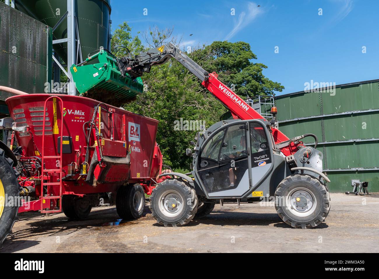 Farmer filling a mixer wagon, which mixes different feeds to make a ...