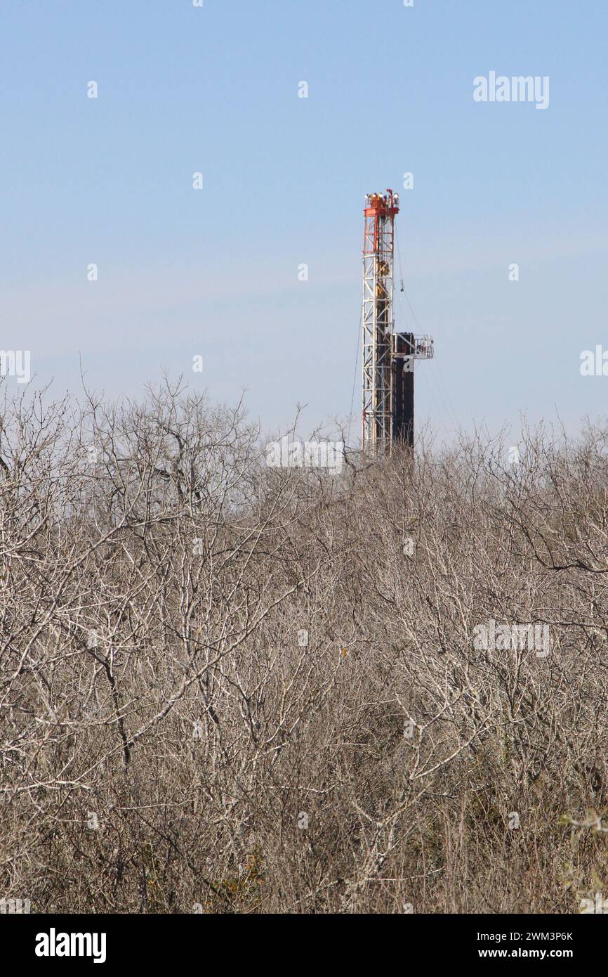 An onshore land oil rig towers over South Texas brush and trees near ...