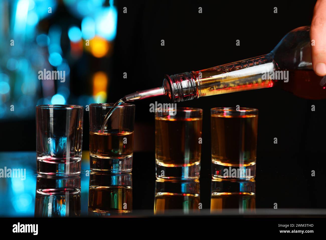 Pouring alcohol drink from bottle into shot glass at mirror bar counter ...