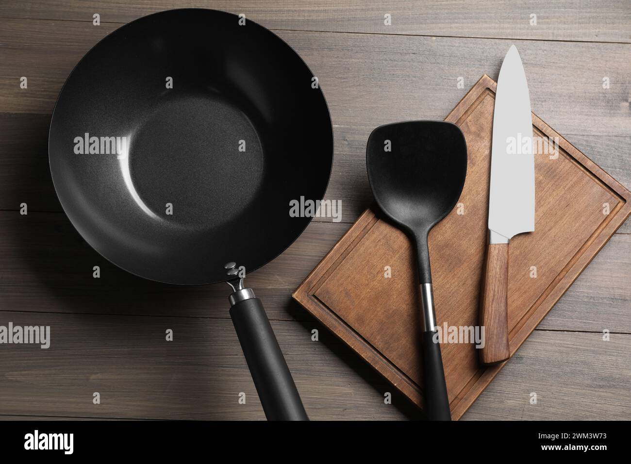 Black metal wok, knife, board and spatula on wooden table, top view ...
