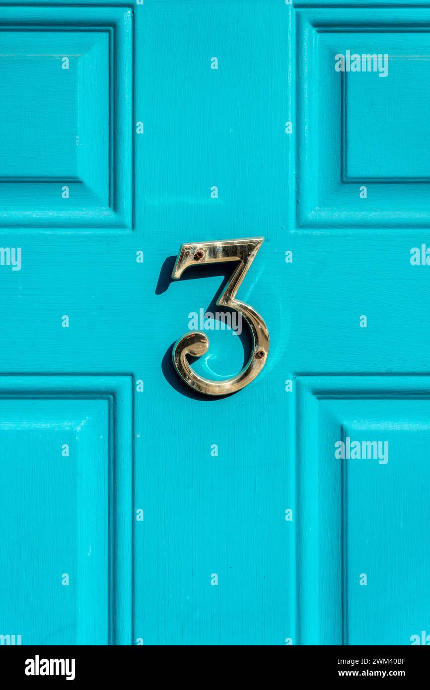 Brass number three on a teal door with shiny reflection and a subtle ...