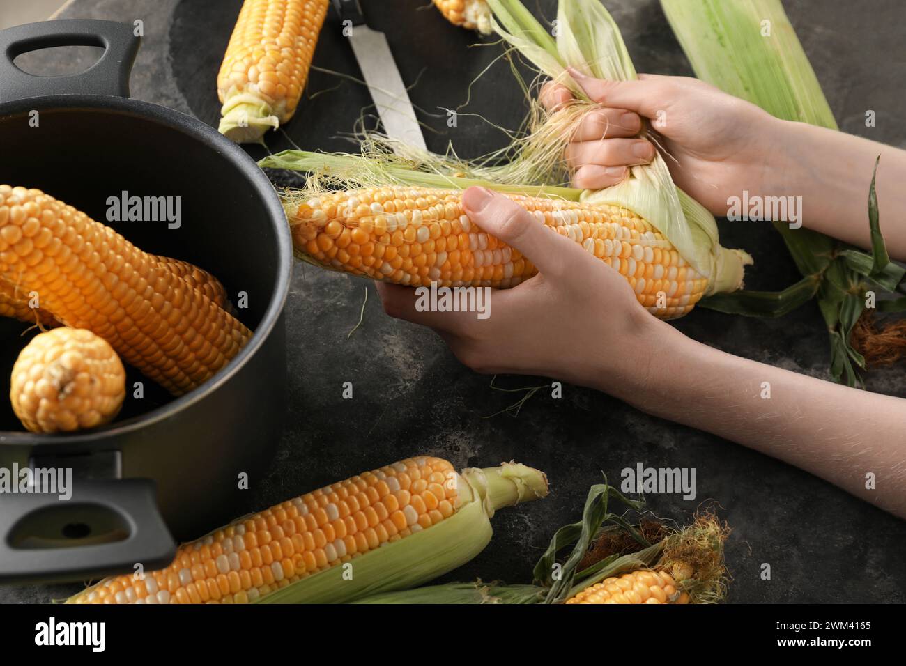 Woman peeling fresh corn cob on black background Stock Photo - Alamy
