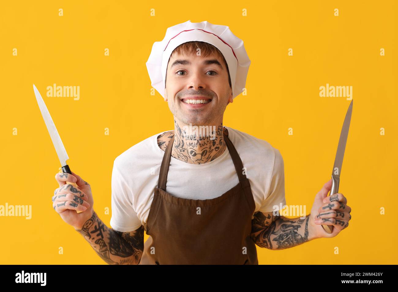 Tattooed happy male chef with knives on yellow background Stock Photo ...