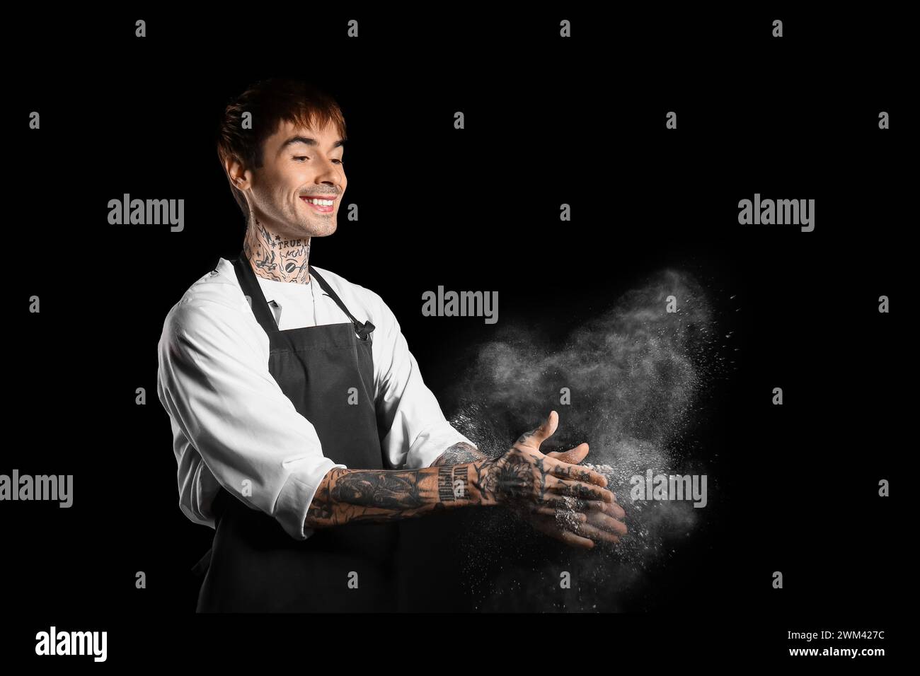 Tattooed happy male chef clapping hands with flour on black background ...