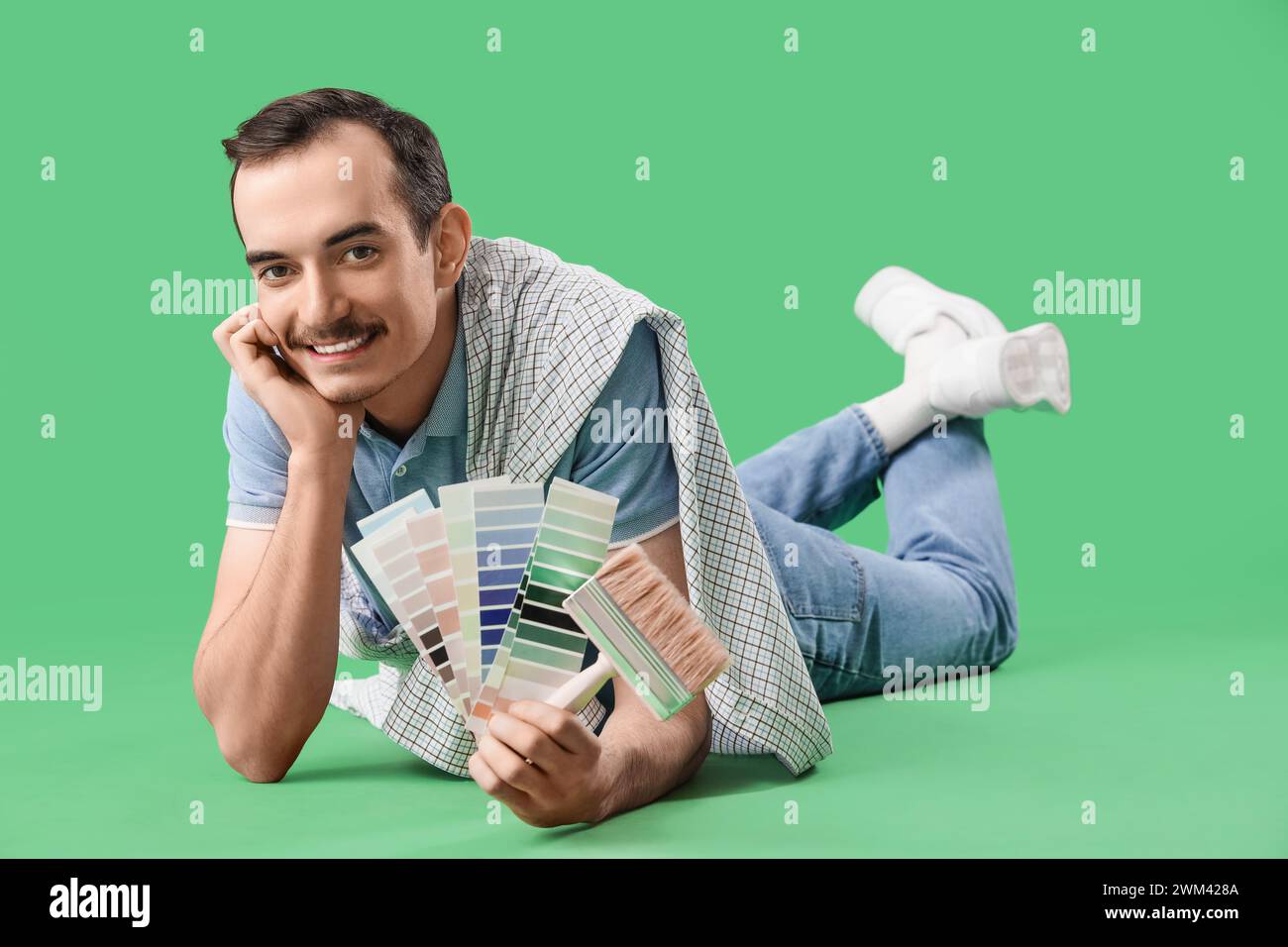 Young man with paint color palettes lying on green background Stock ...
