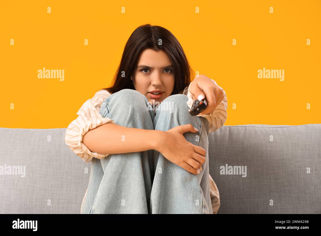 Beautiful young scared woman sitting on sofa and watching TV against ...