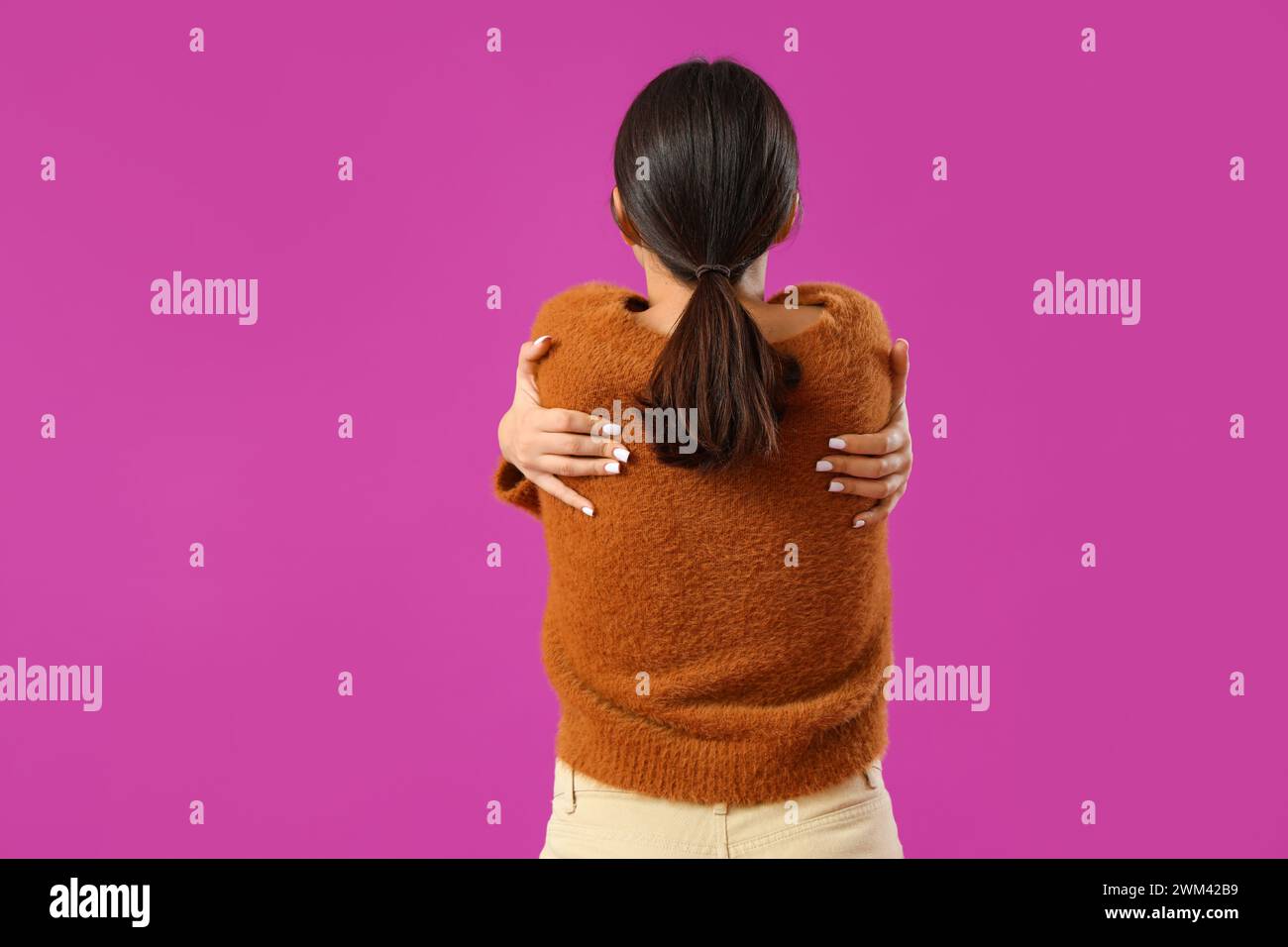 Beautiful young woman hugging herself on purple background, back view ...