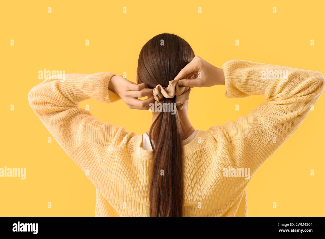 Beautiful young woman with silk scrunchy on ponytail against yellow ...