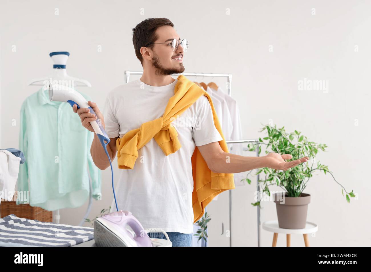 Happy young man with steamer pointing at something in laundry room ...