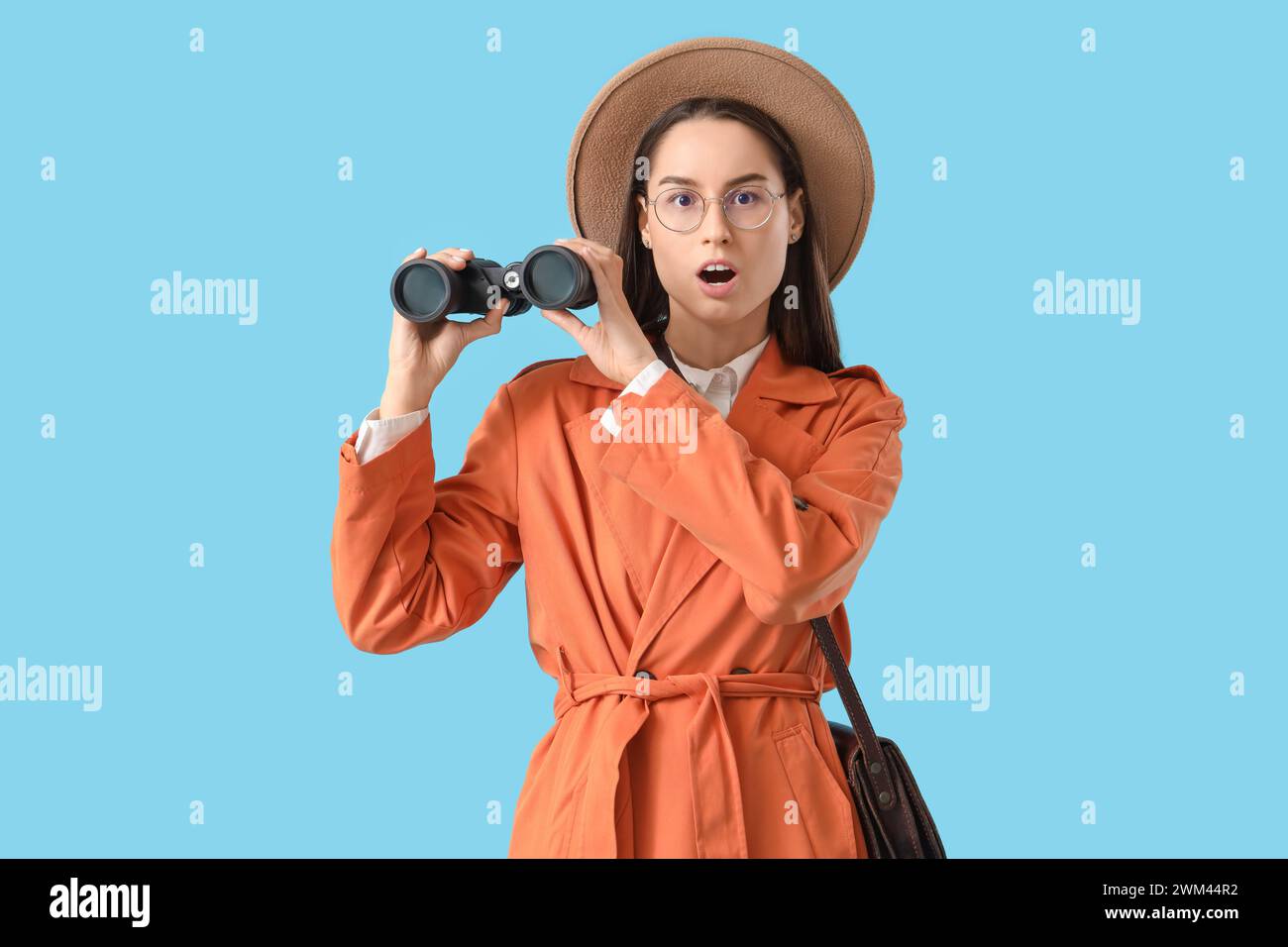 Shocked female detective with binoculars on blue background Stock Photo ...