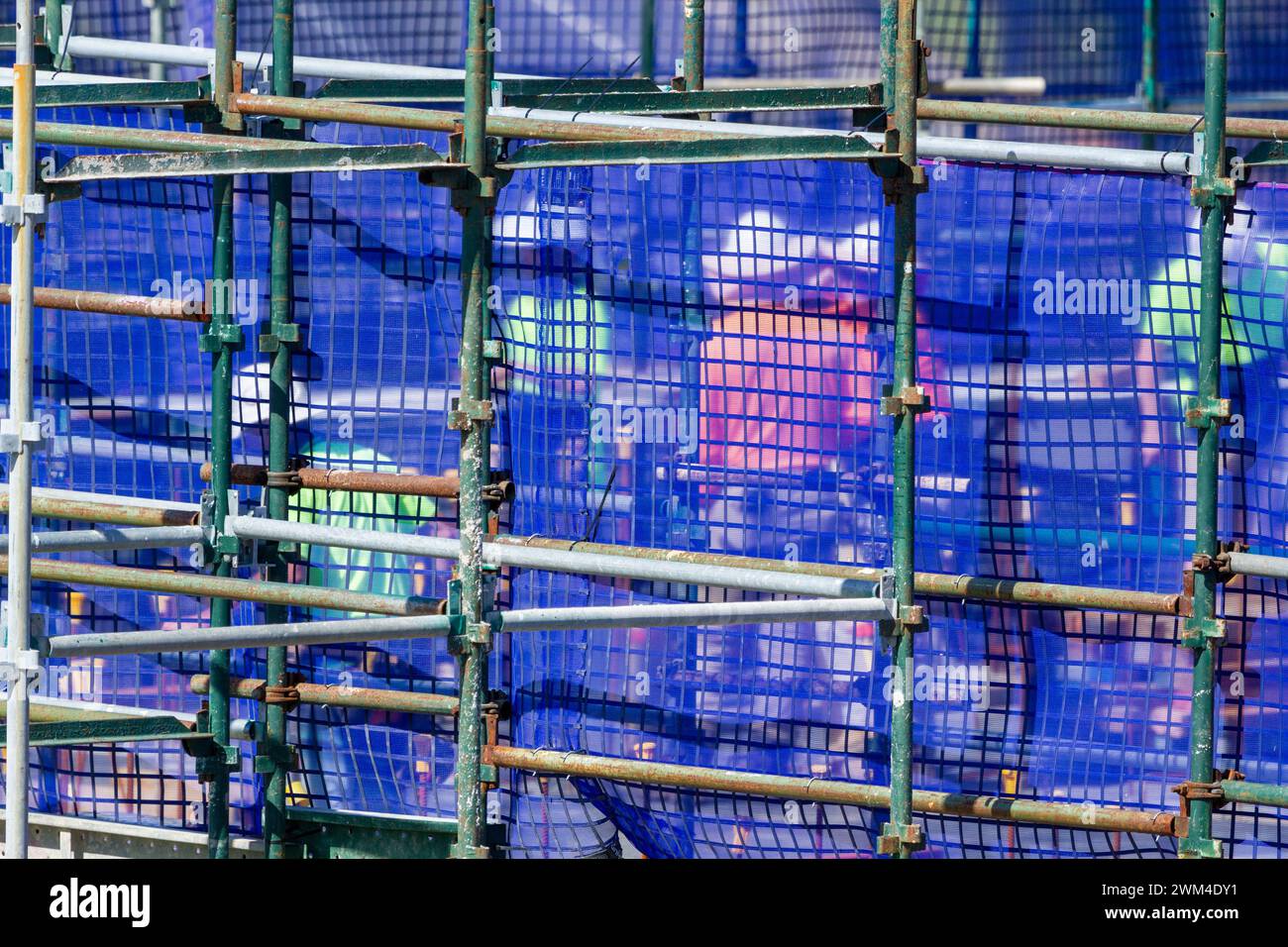 Construction workers behind blue mesh and scaffolding on high rise ...